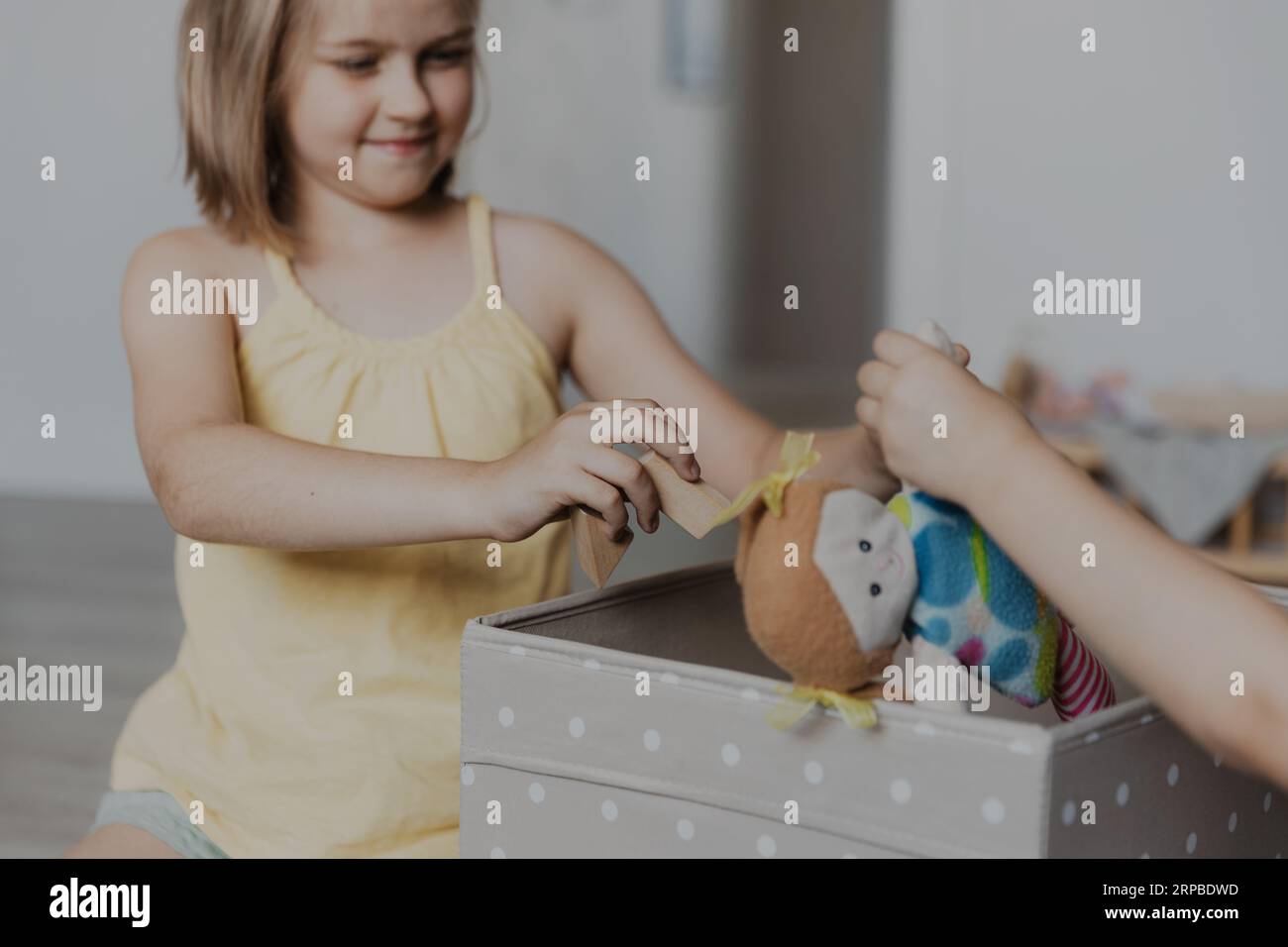 Children cleaning toys from floor after playing, sister helping to ...