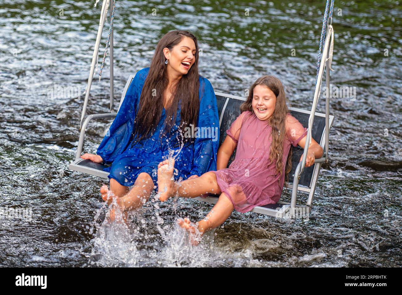 laughing woman and a young girl swing over a fast-flowing river ...