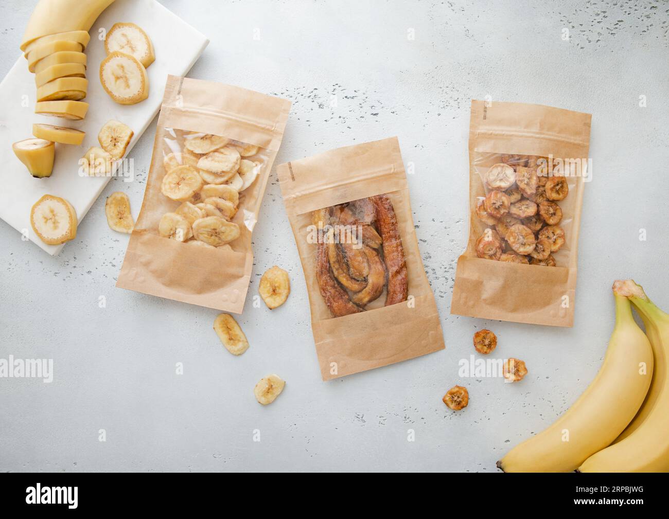 Packages of various crunchy and chewy banana slices with raw bananas on ...