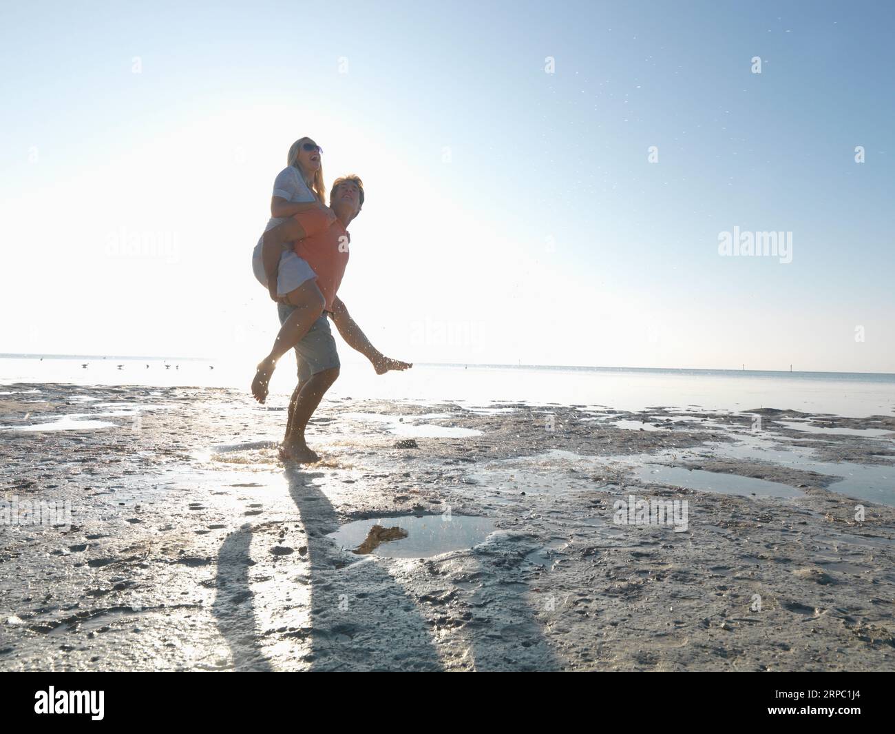 Couple piggyback along beach Stock Photo - Alamy