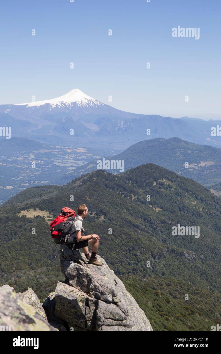 Hiker sits on rock promentory with volcano in distance Stock Photo - Alamy