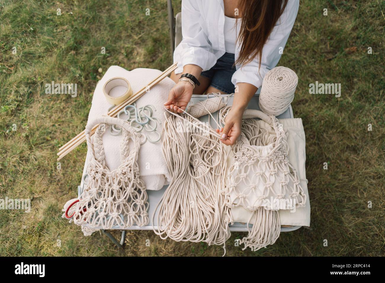 Woman knits bag using macrame technique outdoors near tents. Outdoor ...
