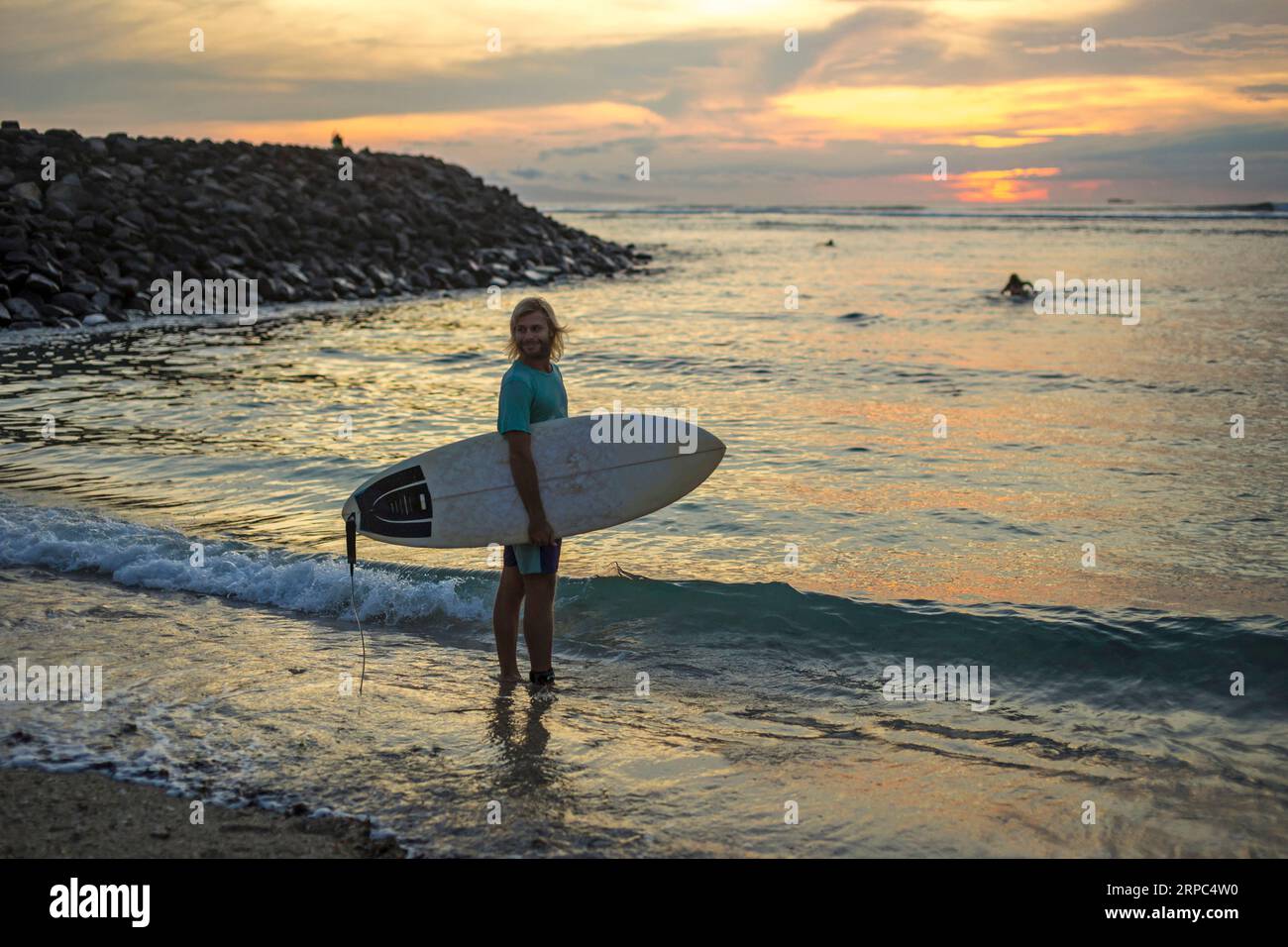 A Surfer stands in ankle-deep water at sunset Stock Photo - Alamy
