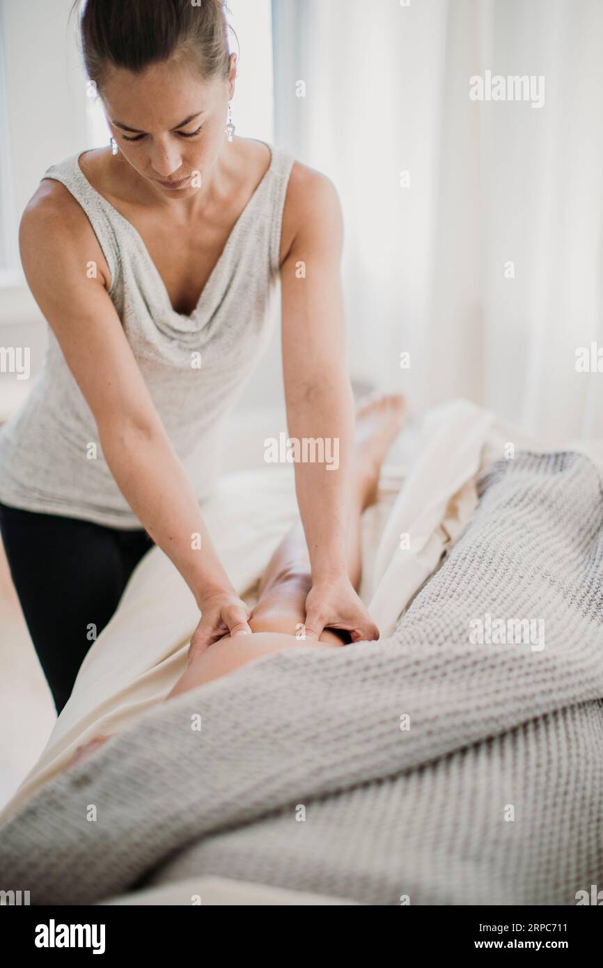 A female massage therapist treats the quadricep of one of her clients ...