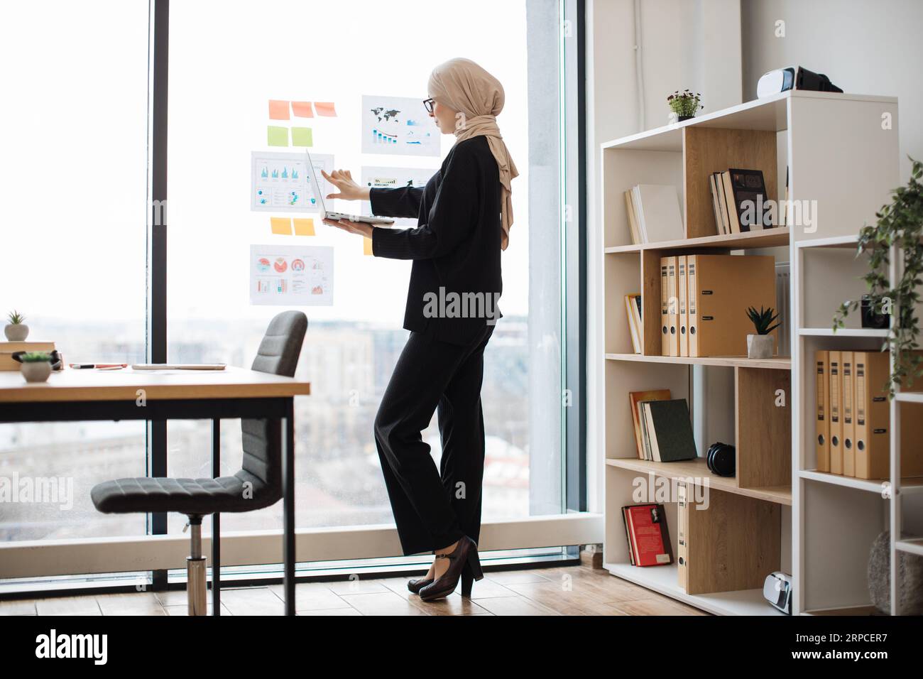 Full length view of stylish muslim lady operating laptop while ...