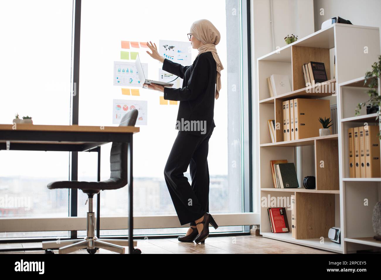 Full length view of stylish muslim lady operating laptop while ...
