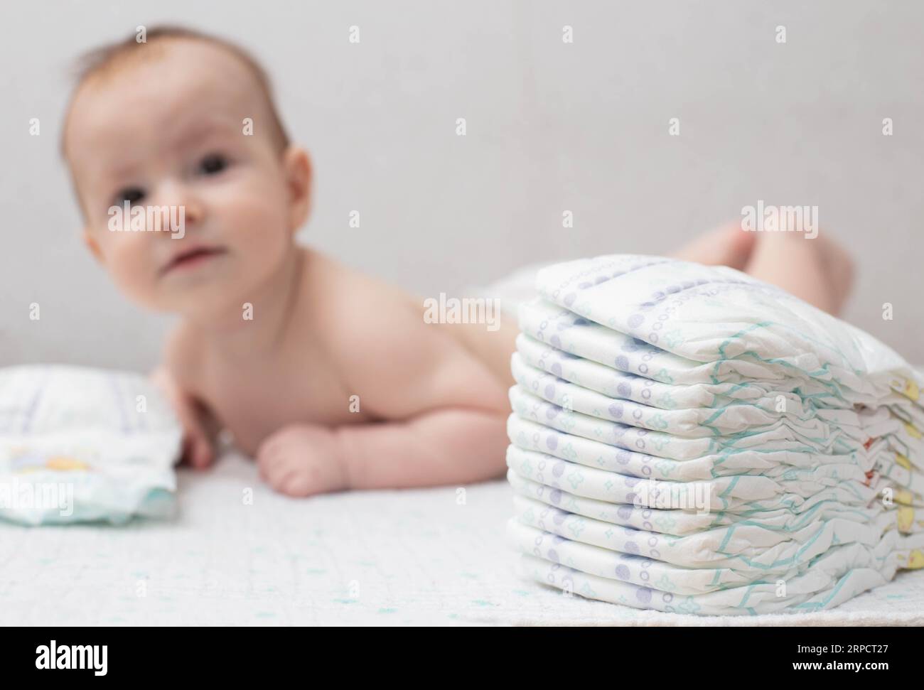 A little boy at the age of 5 months lies in a diaper on a white ...