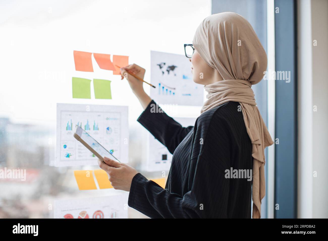 Lady noting down from tablet on paper stickers near charts Stock Photo ...