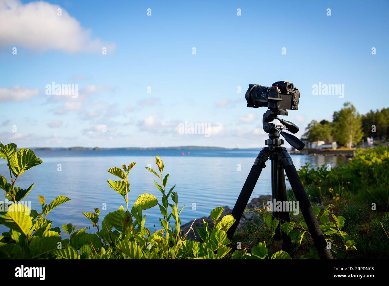 camera mounted on tripod at beautiful lake scenery during day. blue sky ...