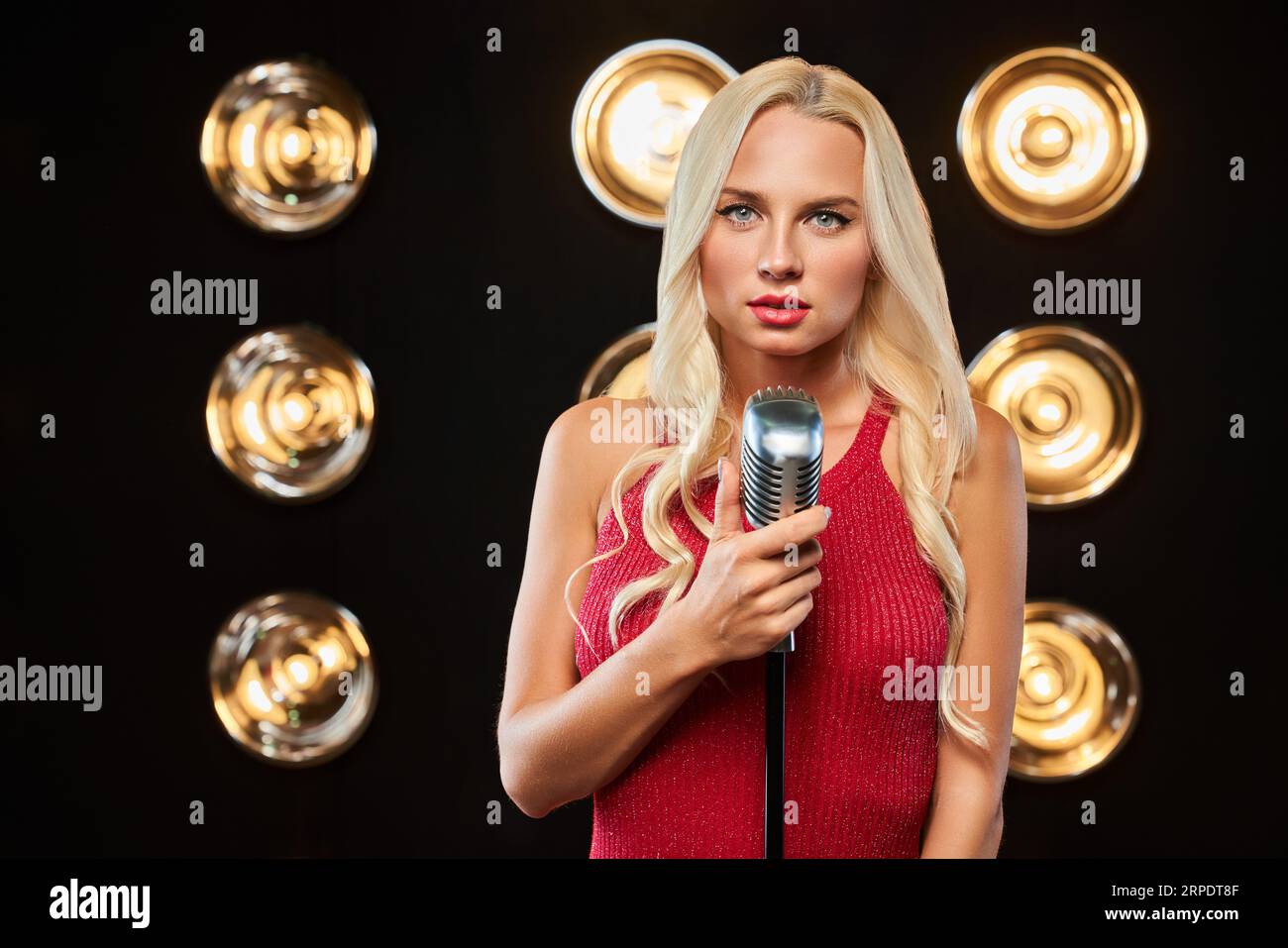 Beautiful blonde girl holding retro microphone, while looking at camera ...