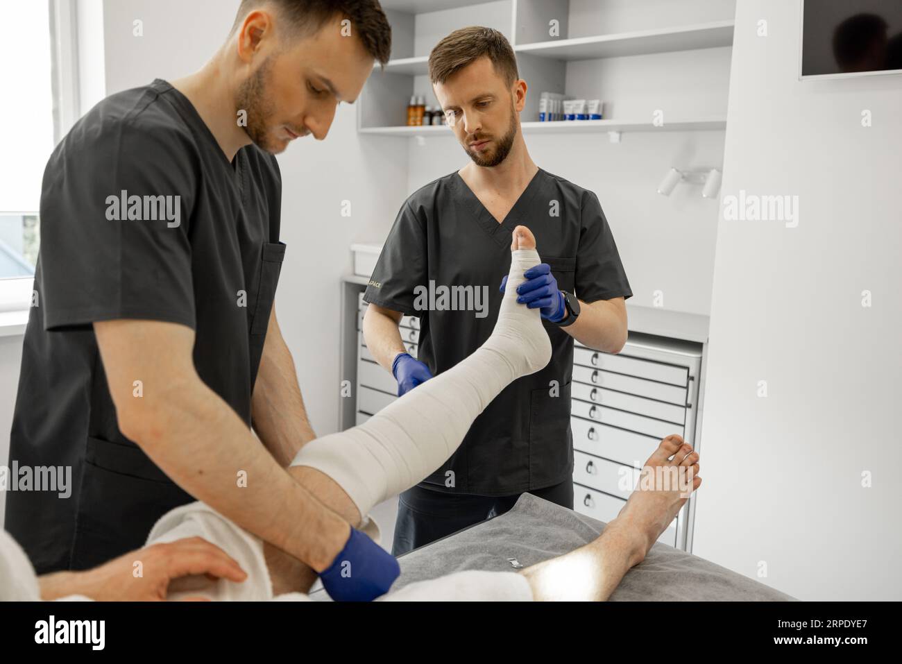 Two medical workers make a bandage on patient's leg Stock Photo - Alamy