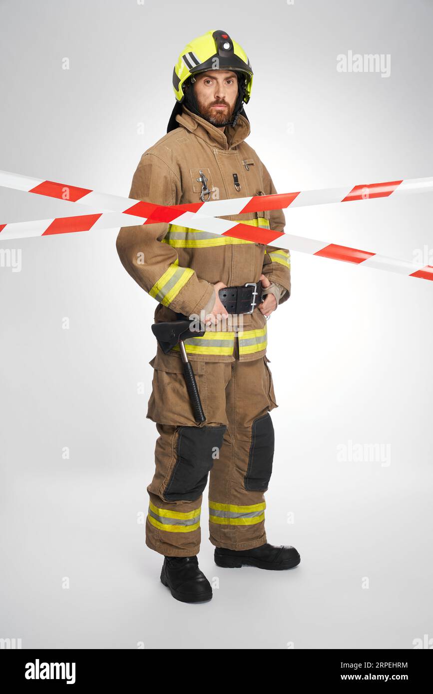 Serious firefighter in full gear standing behind red and white signal ...