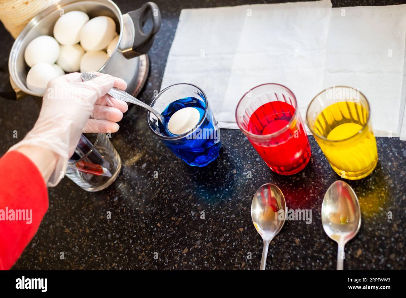 A woman dyes chicken eggs in multi-colored food dyes. Preparing for the ...