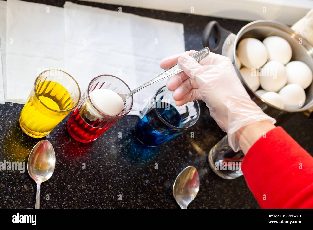 A woman dyes chicken eggs in multi-colored food dyes. Preparing for the ...