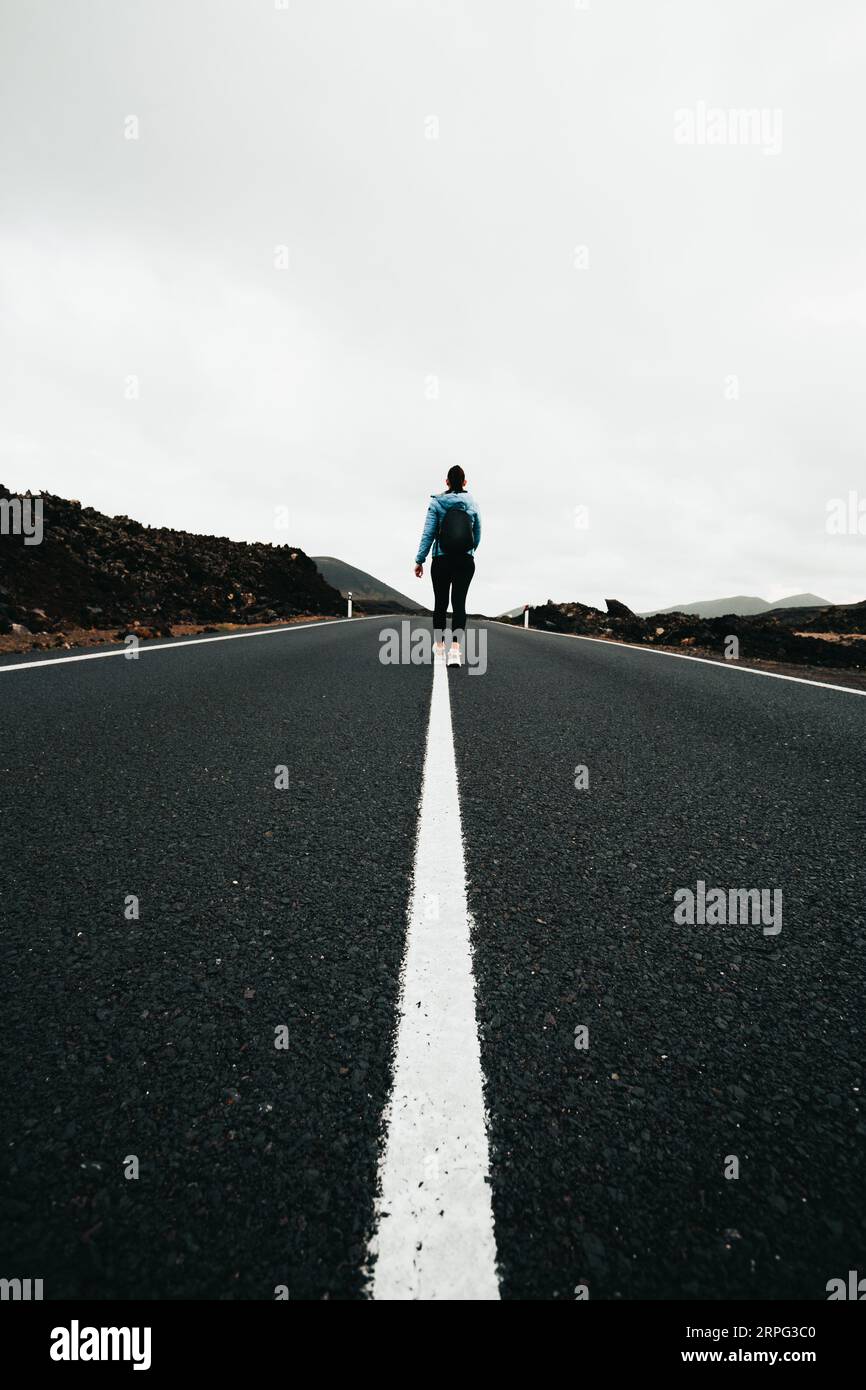 Vertical image of empty road with woman tourist (backpacker) and ...