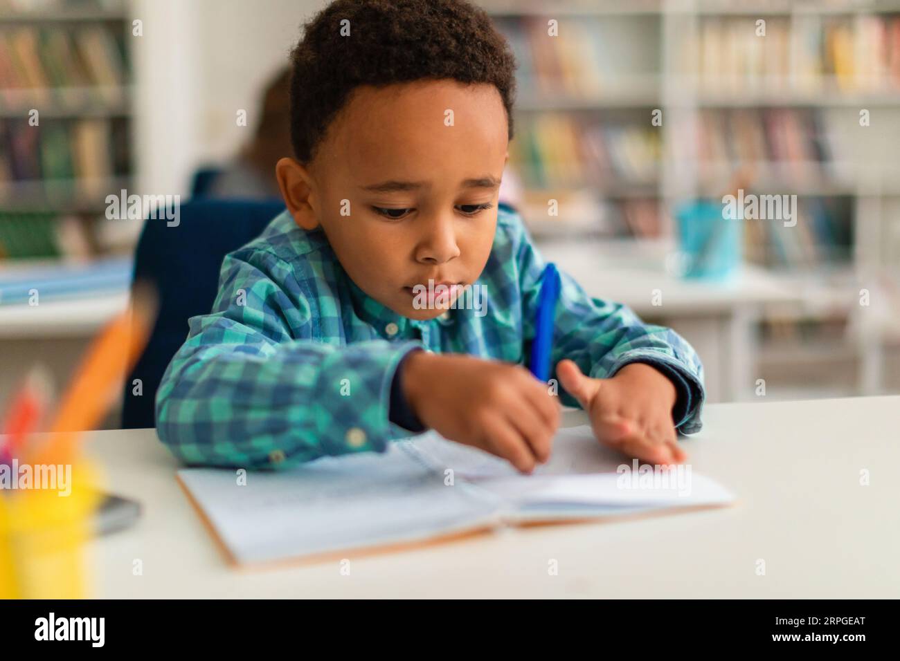 African american pupil boy learning to write in copybook with pen ...