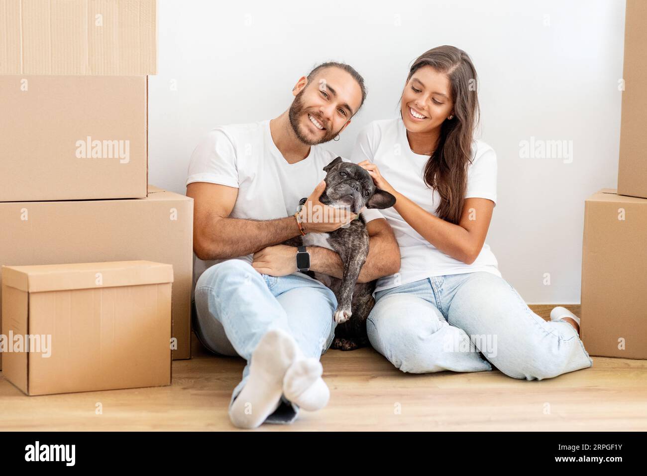 Beautiful young multiracial couple playing with dog, relocation day ...