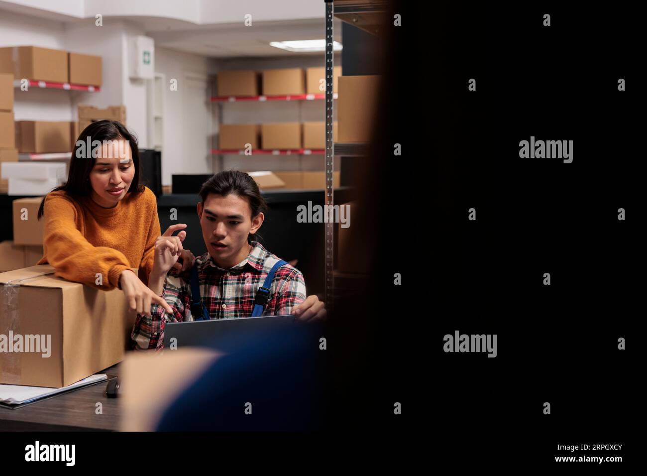 Warehouse package handlers analyzing order pick ticket on laptop while working at storage room ...