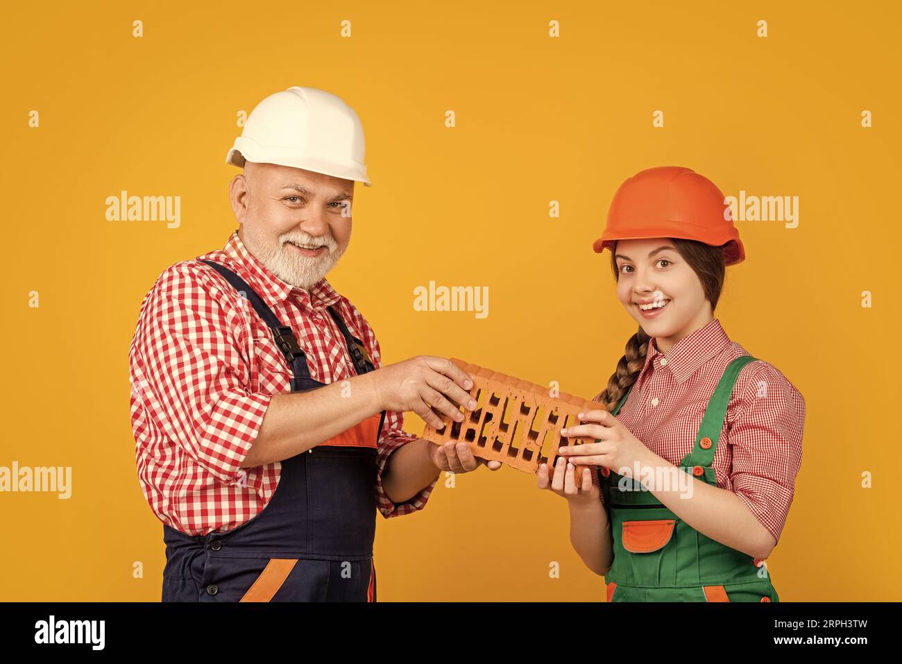 happy teen child and grandfather bricklayer in helmet on yellow ...