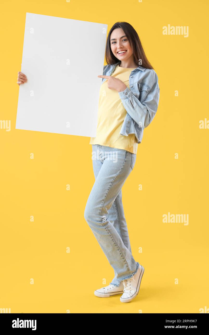 Young woman pointing at big blank poster on yellow background Stock ...