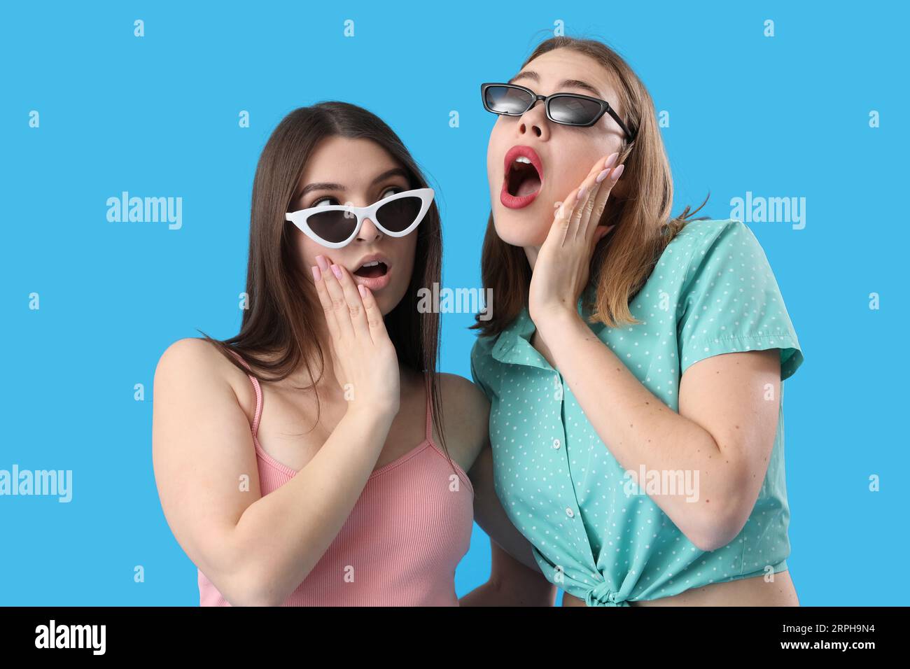 Shocked female friends in sunglasses on blue background Stock Photo - Alamy