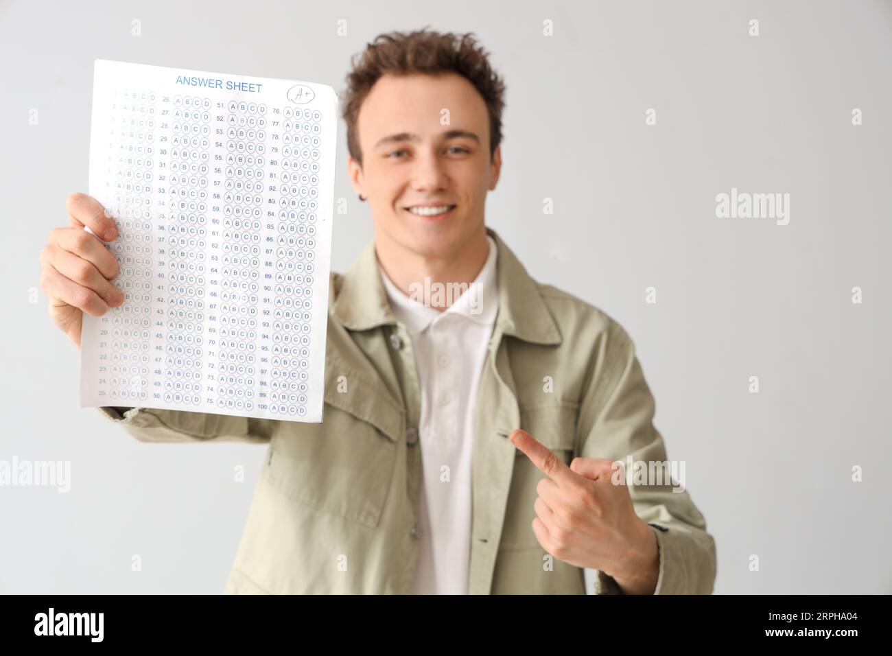 Happy male student pointing at answer sheet for school test on grey ...