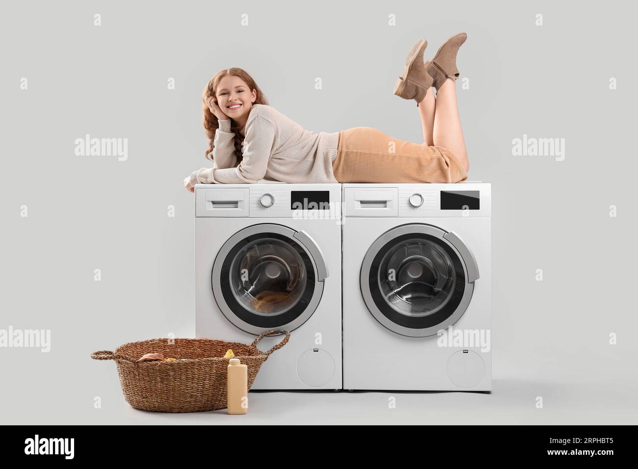 Young woman lying on washing machines against light background Stock ...