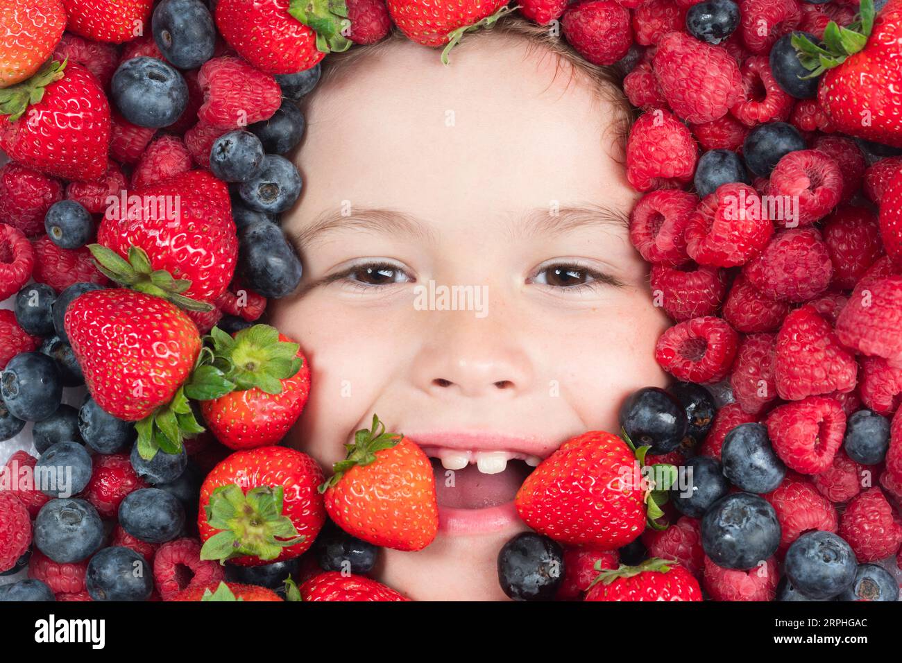 Healthy eating. Kids face with berries mix of strawberry, blueberry ...