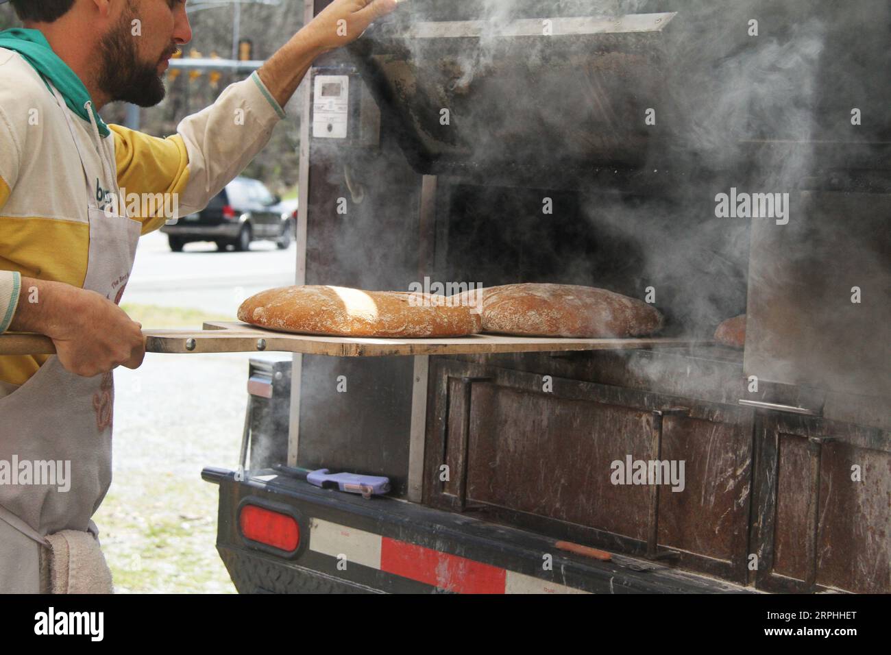 Baker taking fresh loaves of bread out of the outdoor oven Stock Photo ...