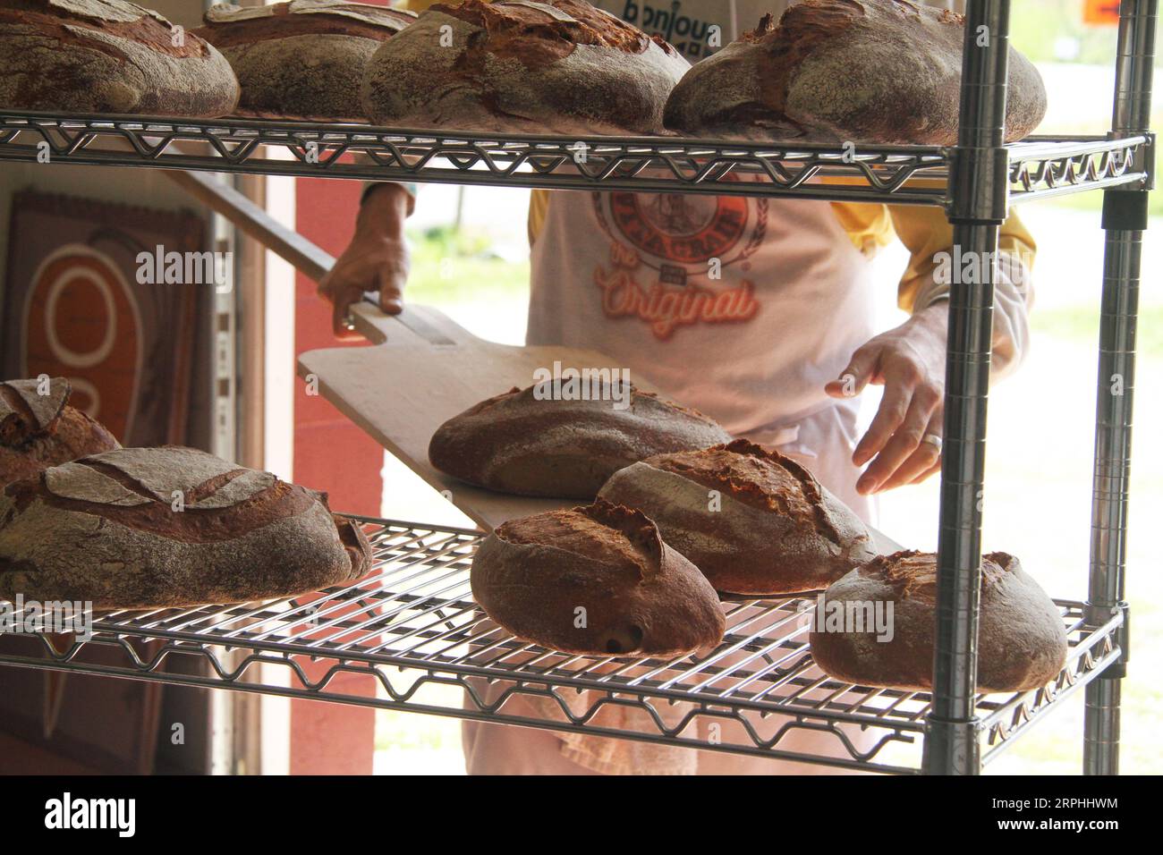 Baker placing fresh loaves of bread on a rack Stock Photo - Alamy