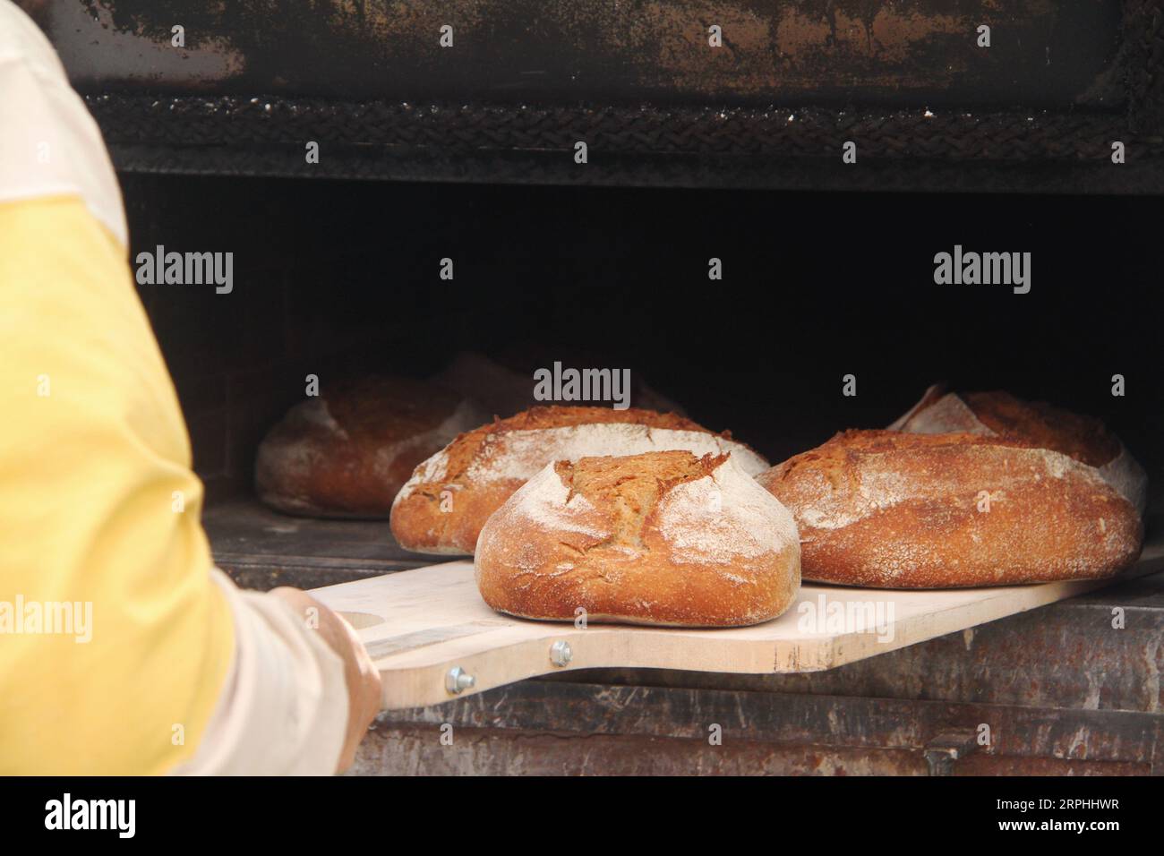 Baker taking fresh loaves of bread out of the oven Stock Photo - Alamy