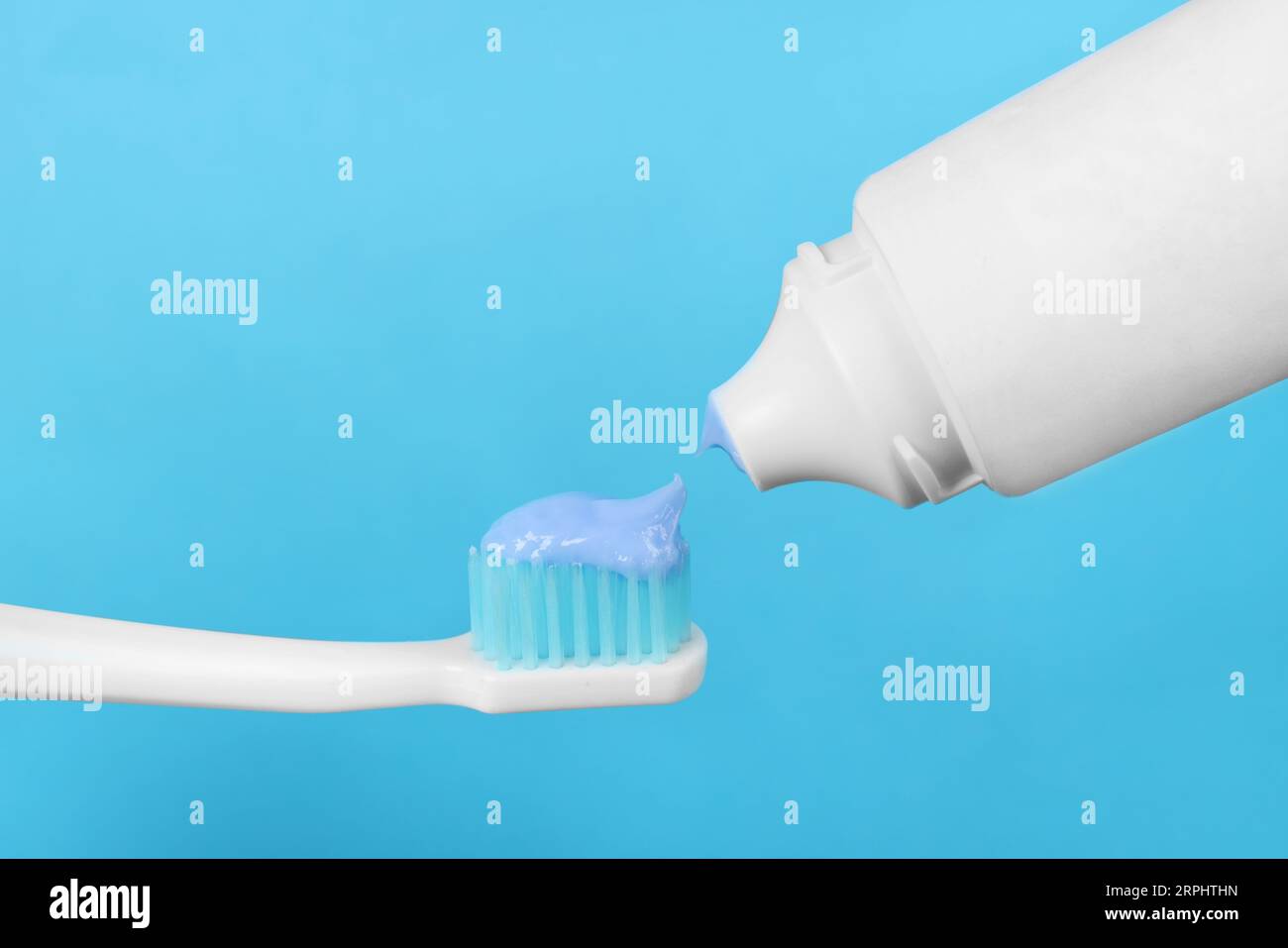 Applying paste on toothbrush against light blue background, closeup ...