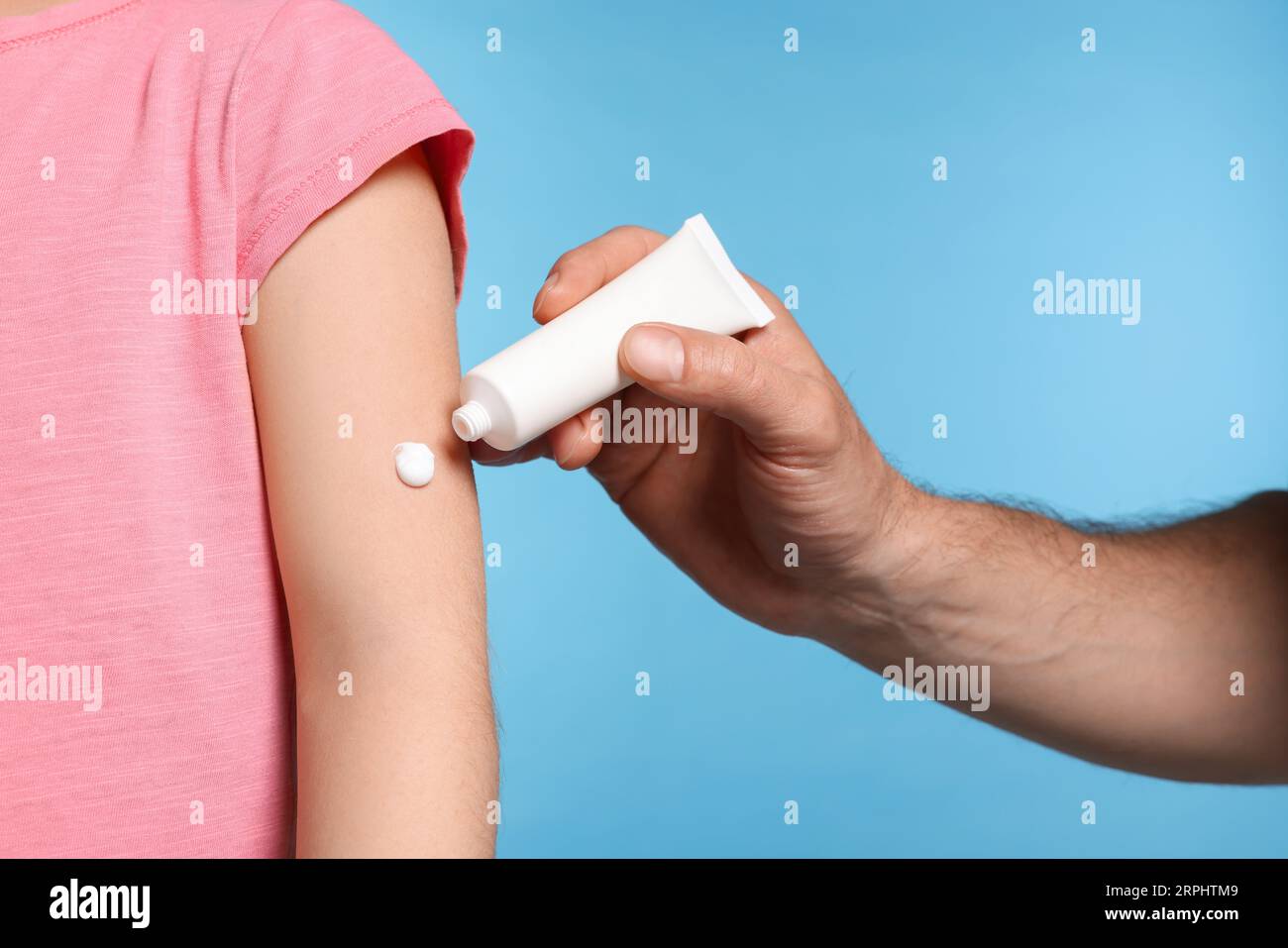 Father applying ointment onto his daughter's arm on light blue ...