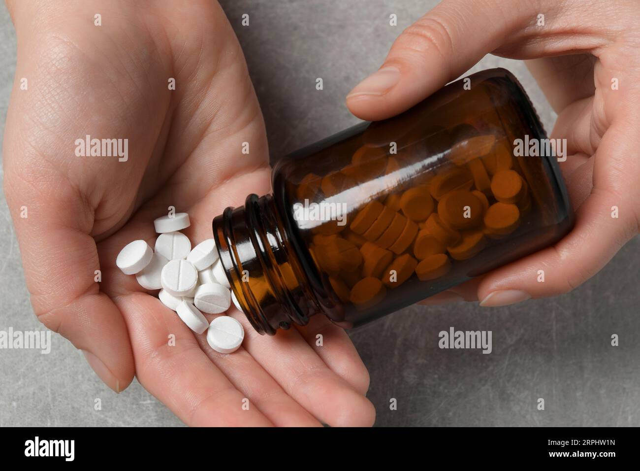 Woman pouring pills from bottle onto hand at light grey table, closeup ...