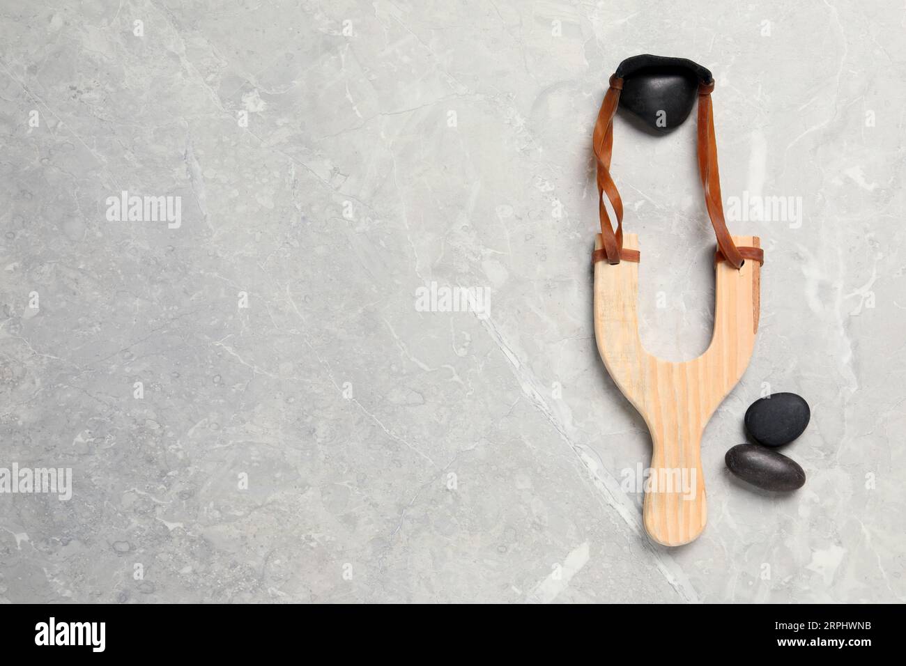 Wooden slingshot with stones on light grey marble background, flat lay ...