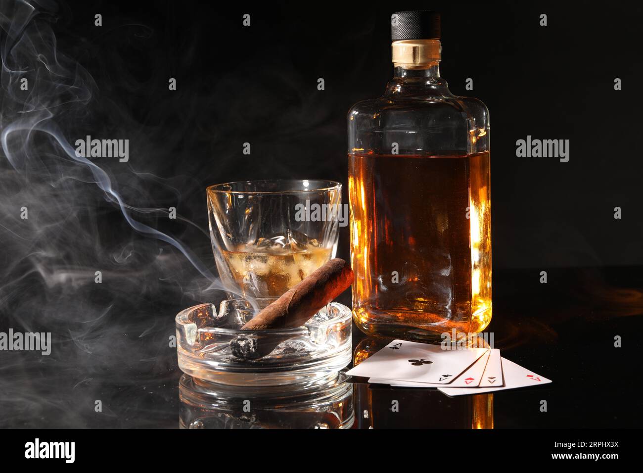 Smoldering cigar, ashtray, playing cards and whiskey on black mirror ...