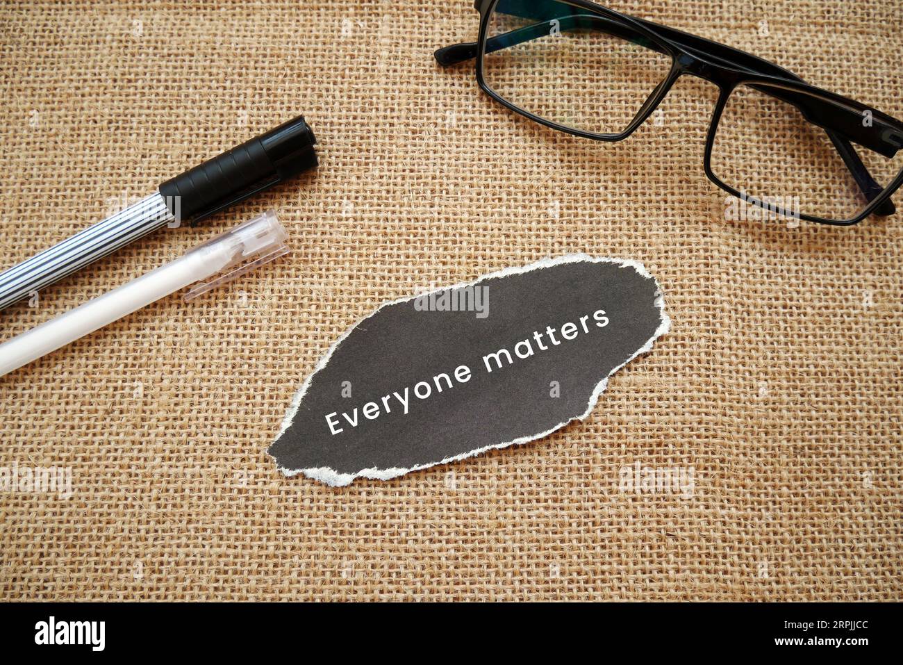 Everyone matters text on torn paper on burlap with alarm clock, glasses ...
