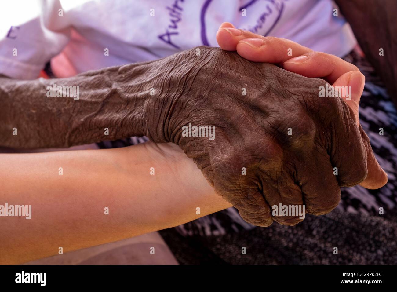 Carers hand caressing the hand of an aged Indigenous woman at an aged ...