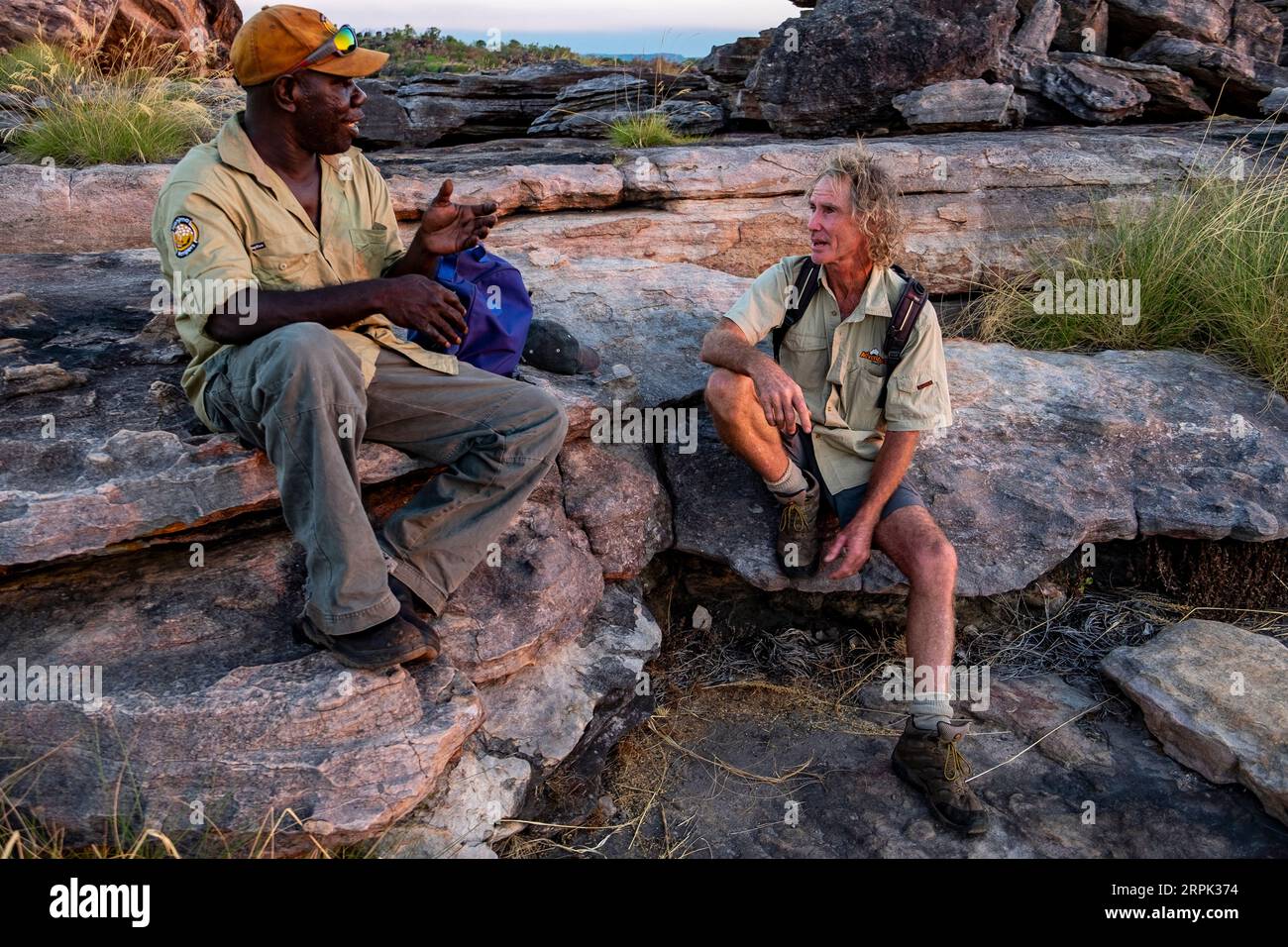 Indigenous and white tour guides exchange information at sunset on the summit of Ubirr Rock in ...