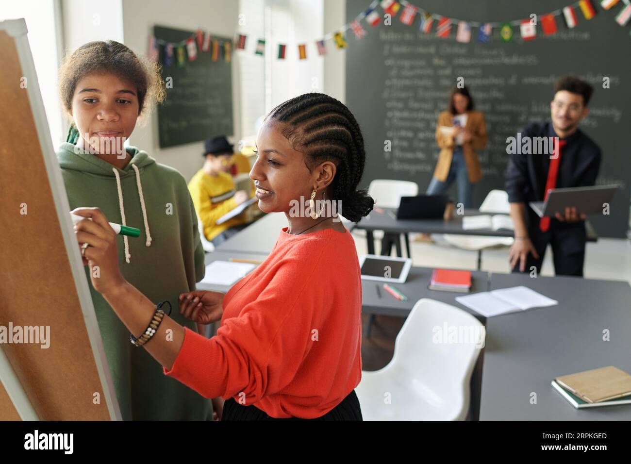 Young African American teacher writing on blackboard and explaining ...