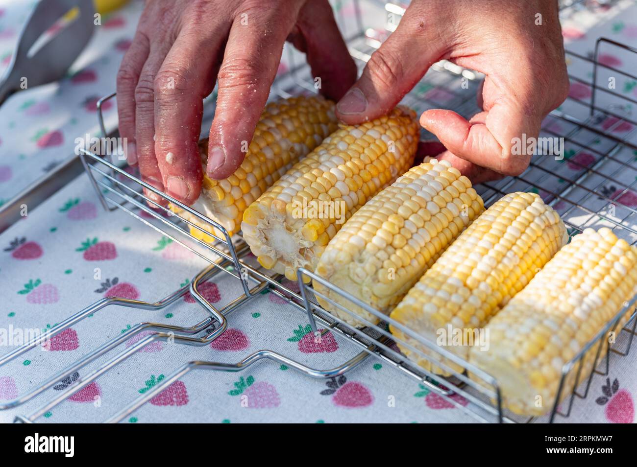 Close-up of fresh young heads of corn on the grill. A man's hand puts ...