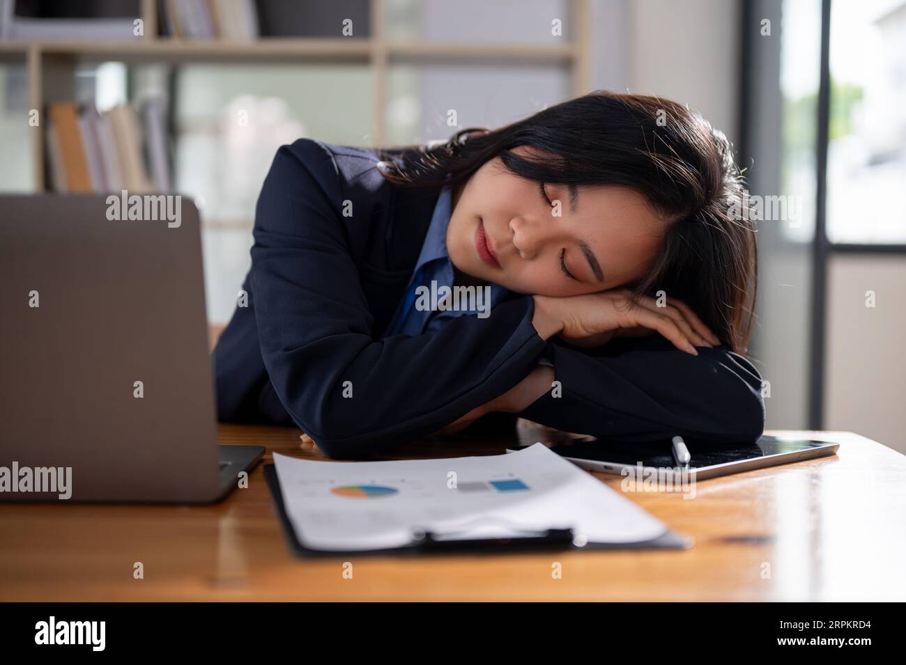 A tired and sleepy young Asian businesswoman or female office worker falls asleep at her desk in ...