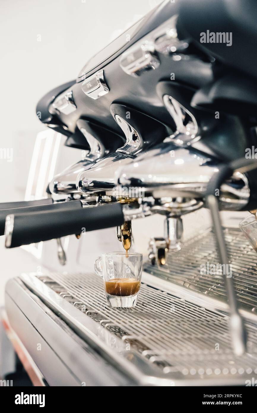 Espresso dripping from portafilter of coffee machine into glass cup ...