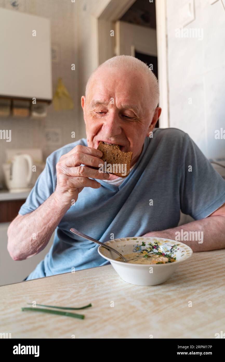 Elderly senior man eating soup with bread and green onion at home in ...