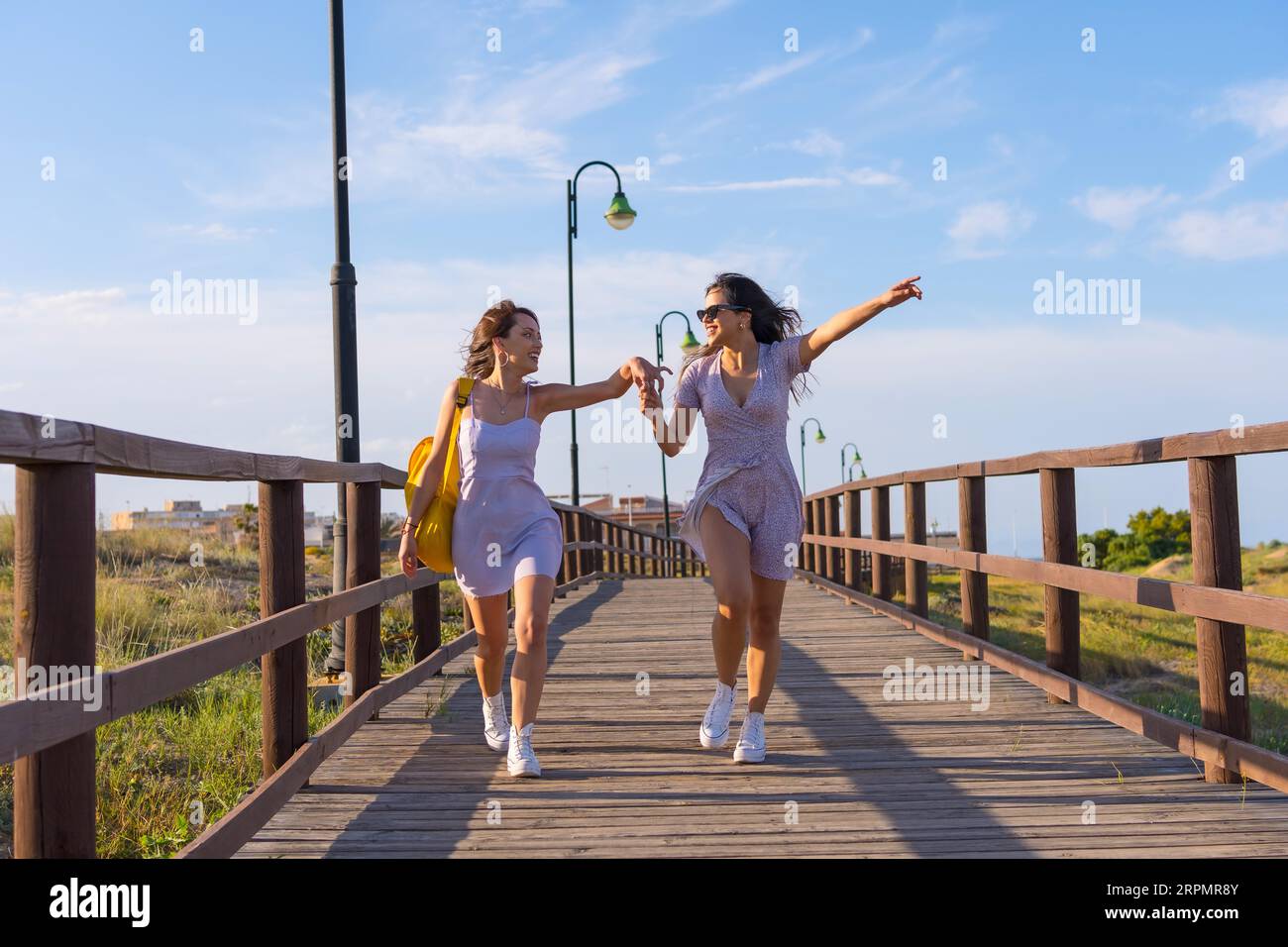 Female friends on summer vacation at the beach walking on a wooden path ...