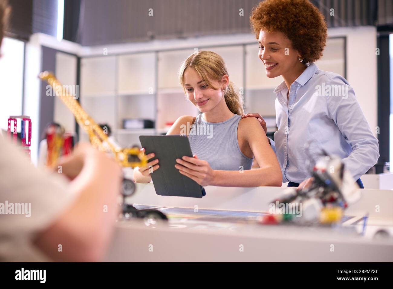 Female High School Teacher With Digital Tablet Helping Teenage Girl In ...