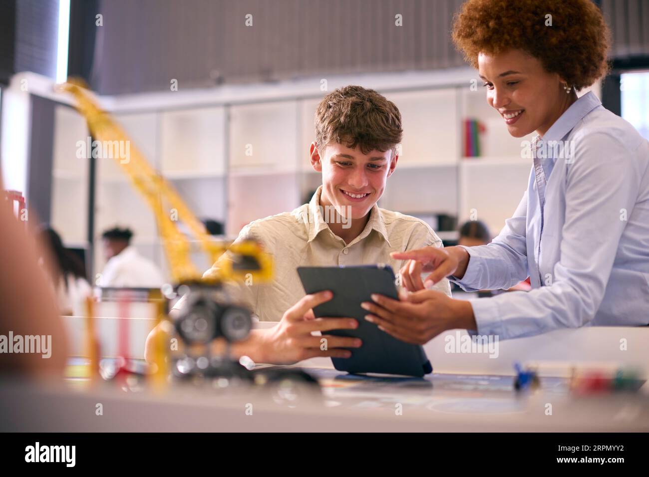 Female High School Teacher With Digital Tablet Helping Teenage Boy In ...