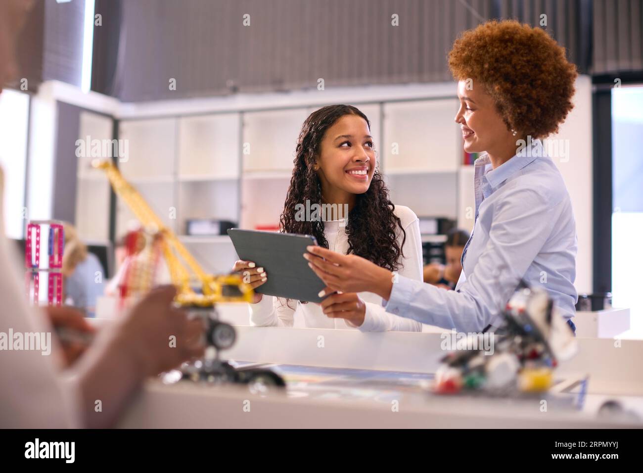 Female High School Teacher With Digital Tablet Helping Teenage Girl In ...