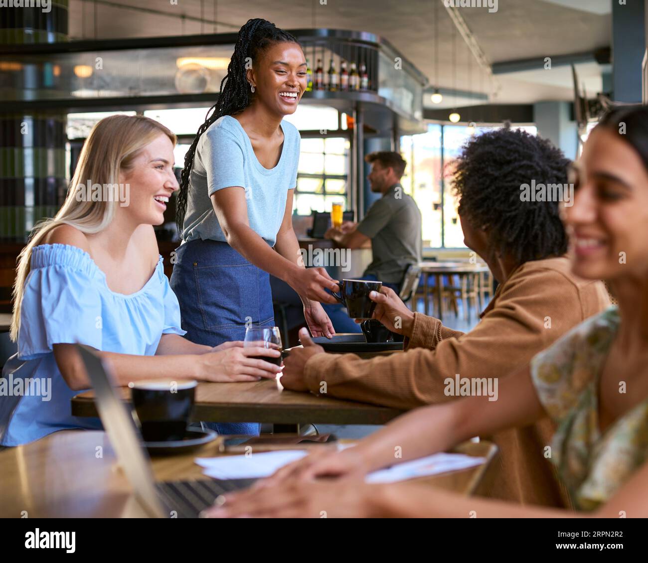Couple Meeting In Busy Coffee Shop Being Served At Table By Waitress ...
