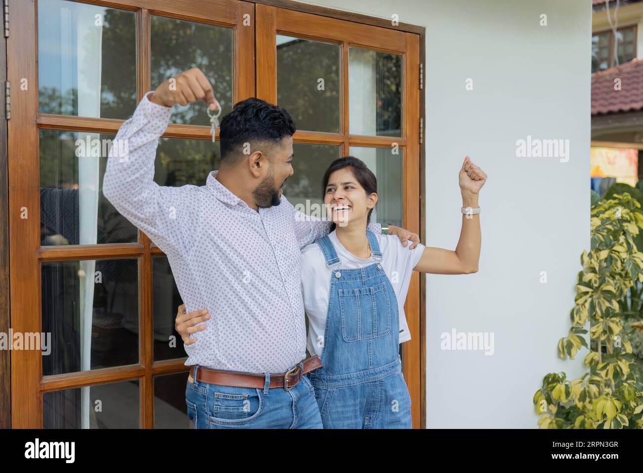 Married Indian couple holding keys and standing outside their new home ...
